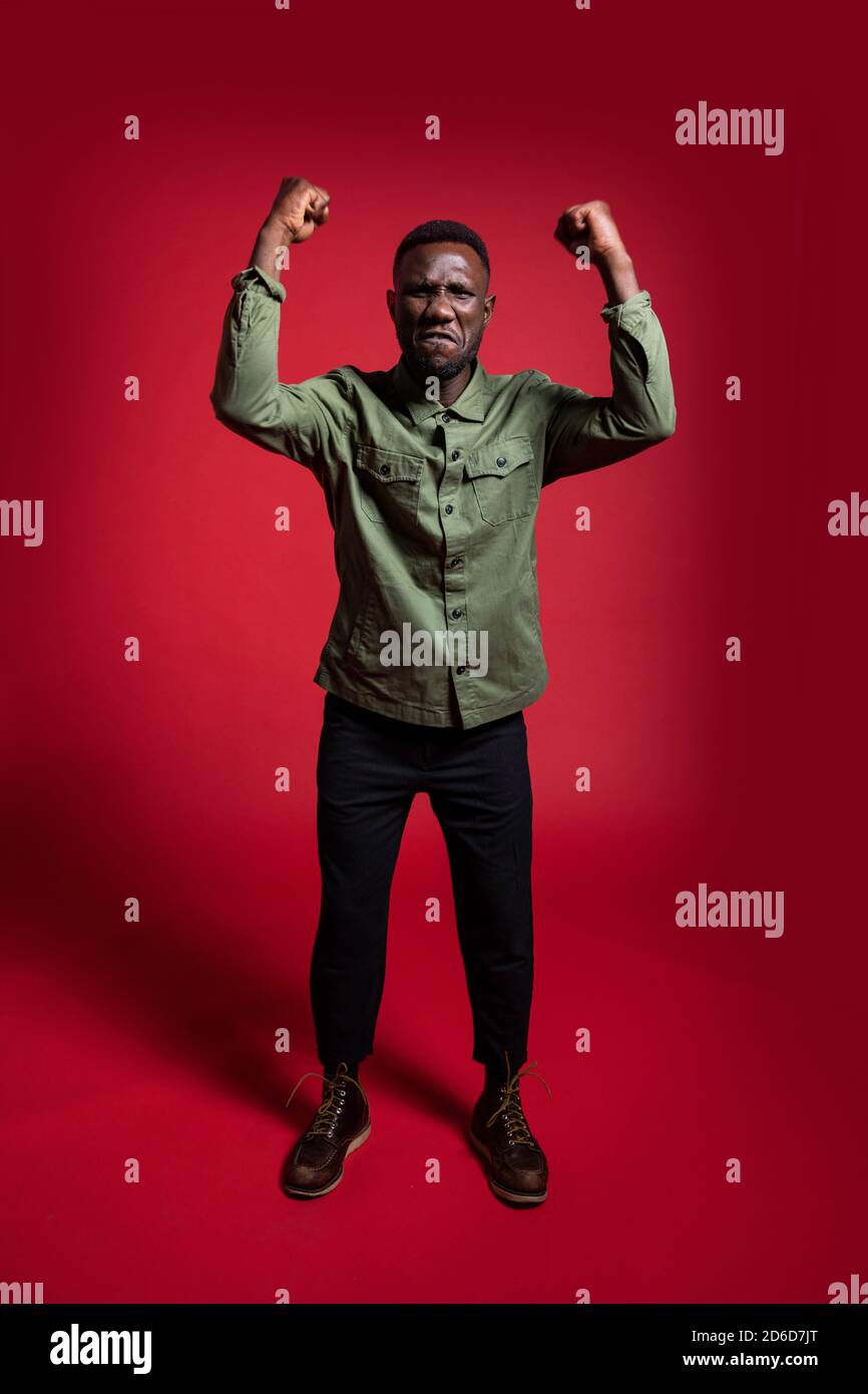 Young black man posing in protest pose with fists clenched and raised ...