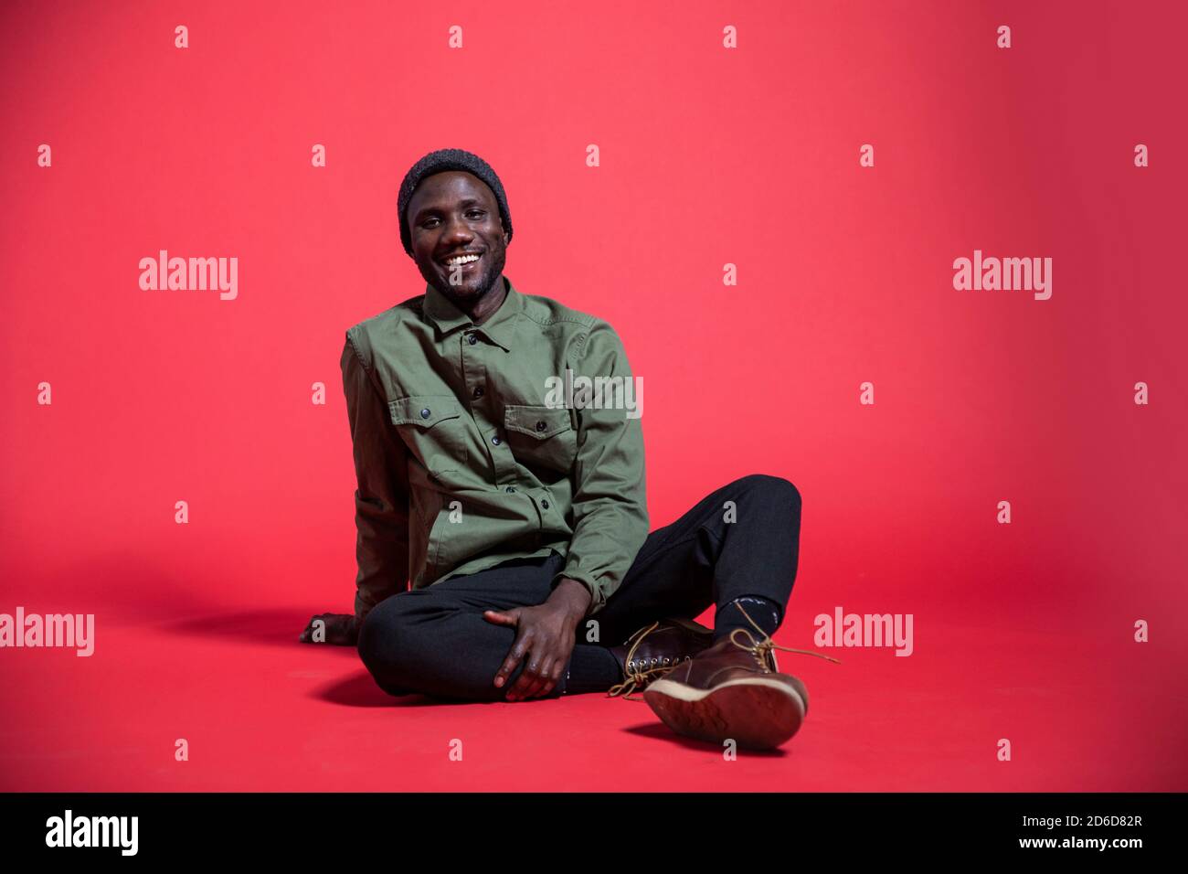 Young black man sitting on floor smiling at camera. Isolated. Full ...