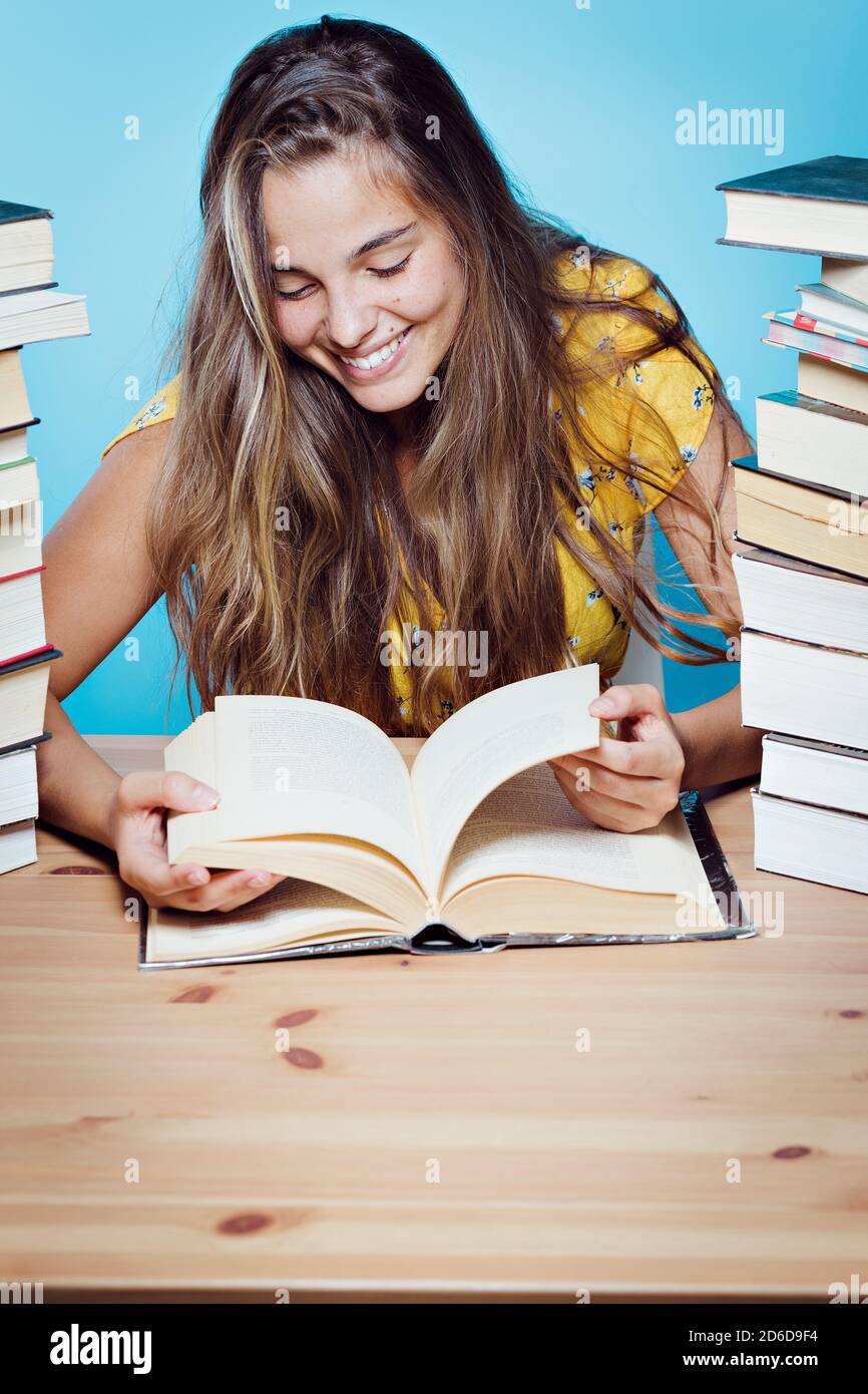 Vertical shot of a smiling young lady reading a book and a stack of ...