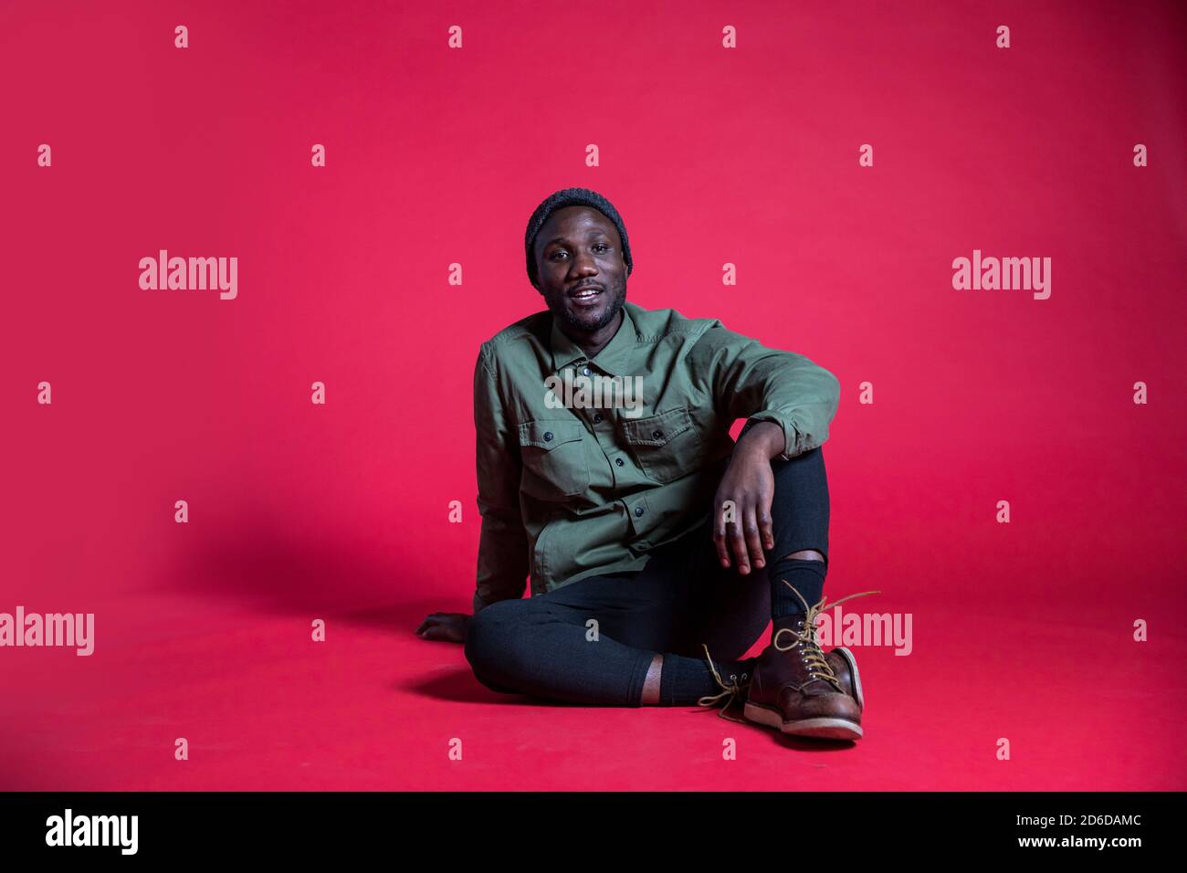 Young black man sitting on studio floor for photoshoot. Isolated. Full ...