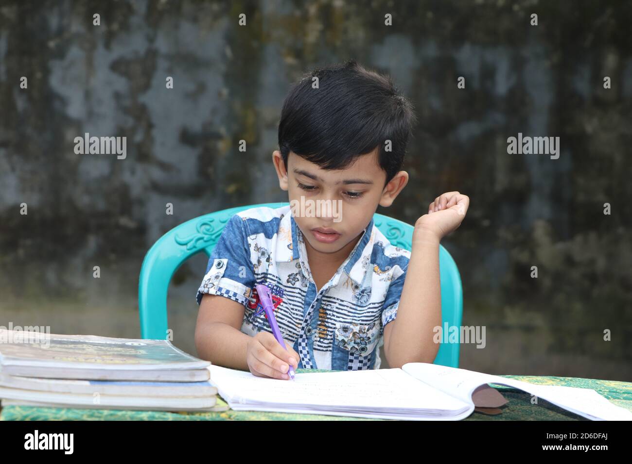 Little asian boy sitting by a desk writing in the notebook. School kid ...