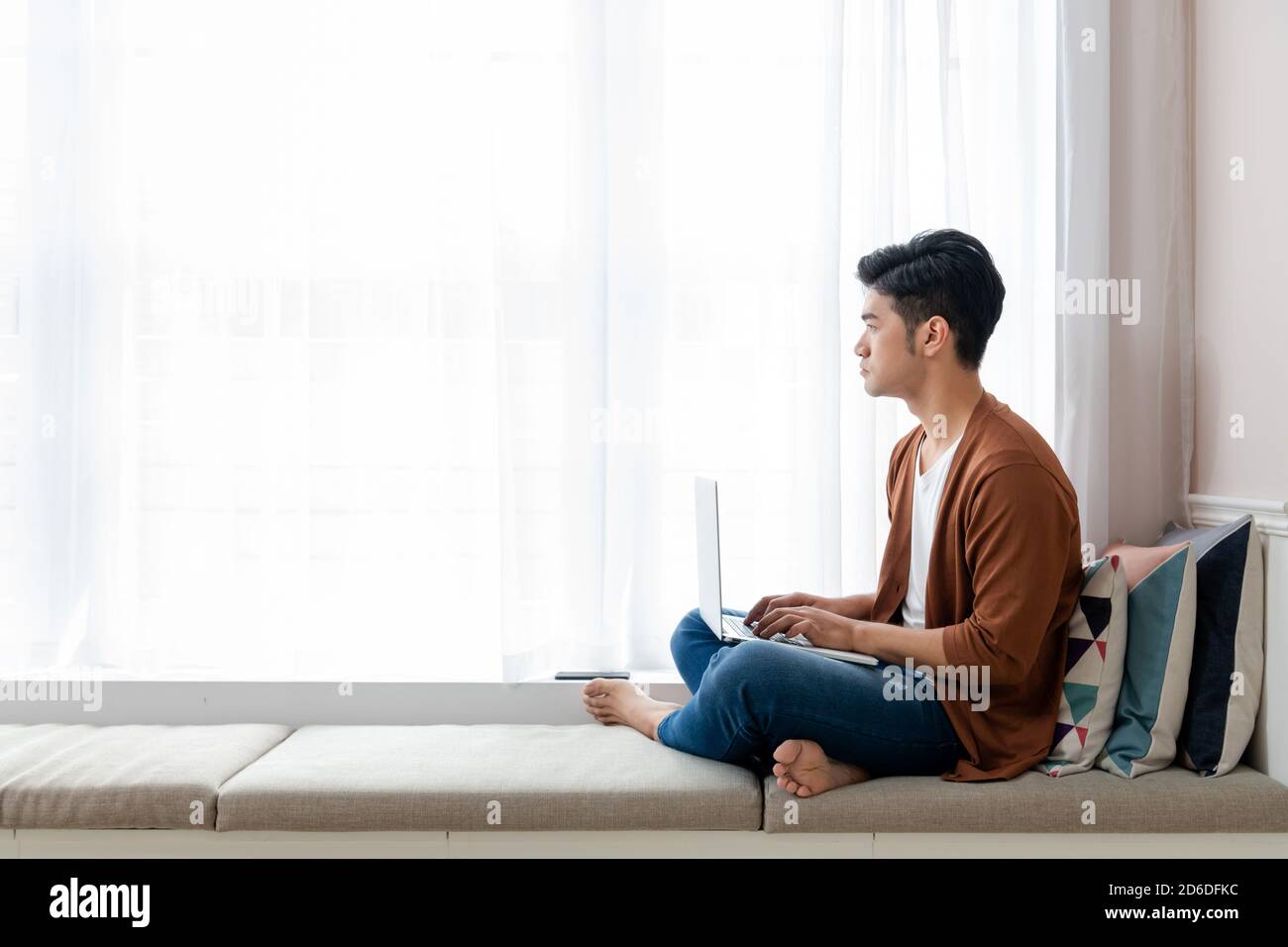 A young man working at home, sitting by the window with a laptop Stock ...