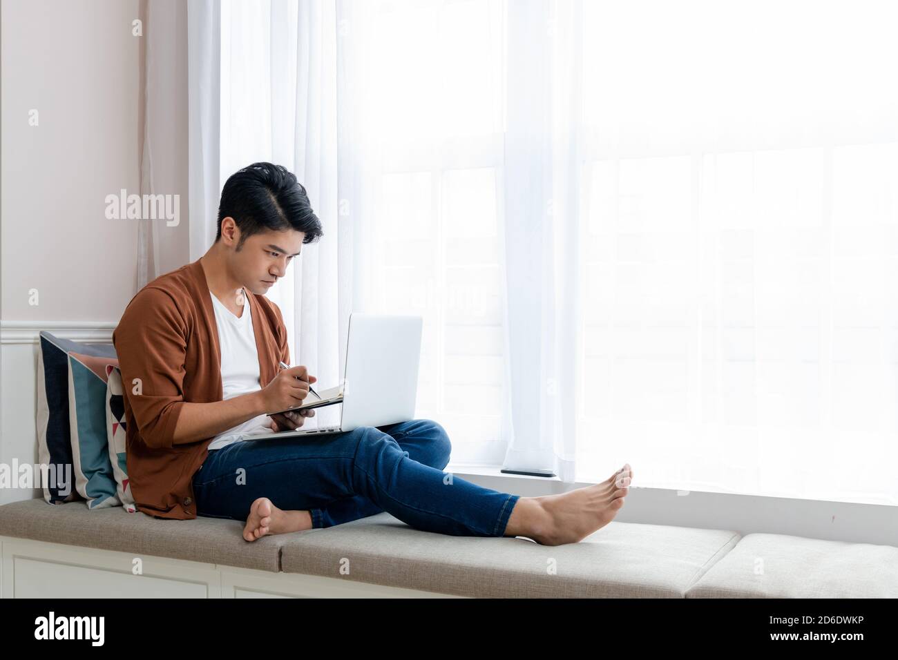 A young man working at home, sitting by the window with a laptop Stock ...