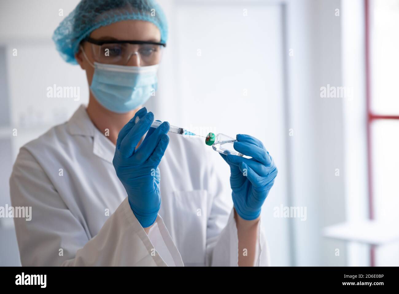 Female doctor wearing face mask injecting syringe into a vial bottle ...