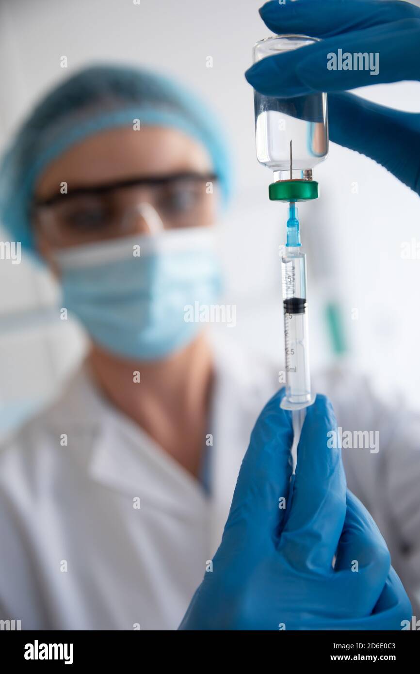Female doctor wearing face mask injecting syringe into a vial bottle ...