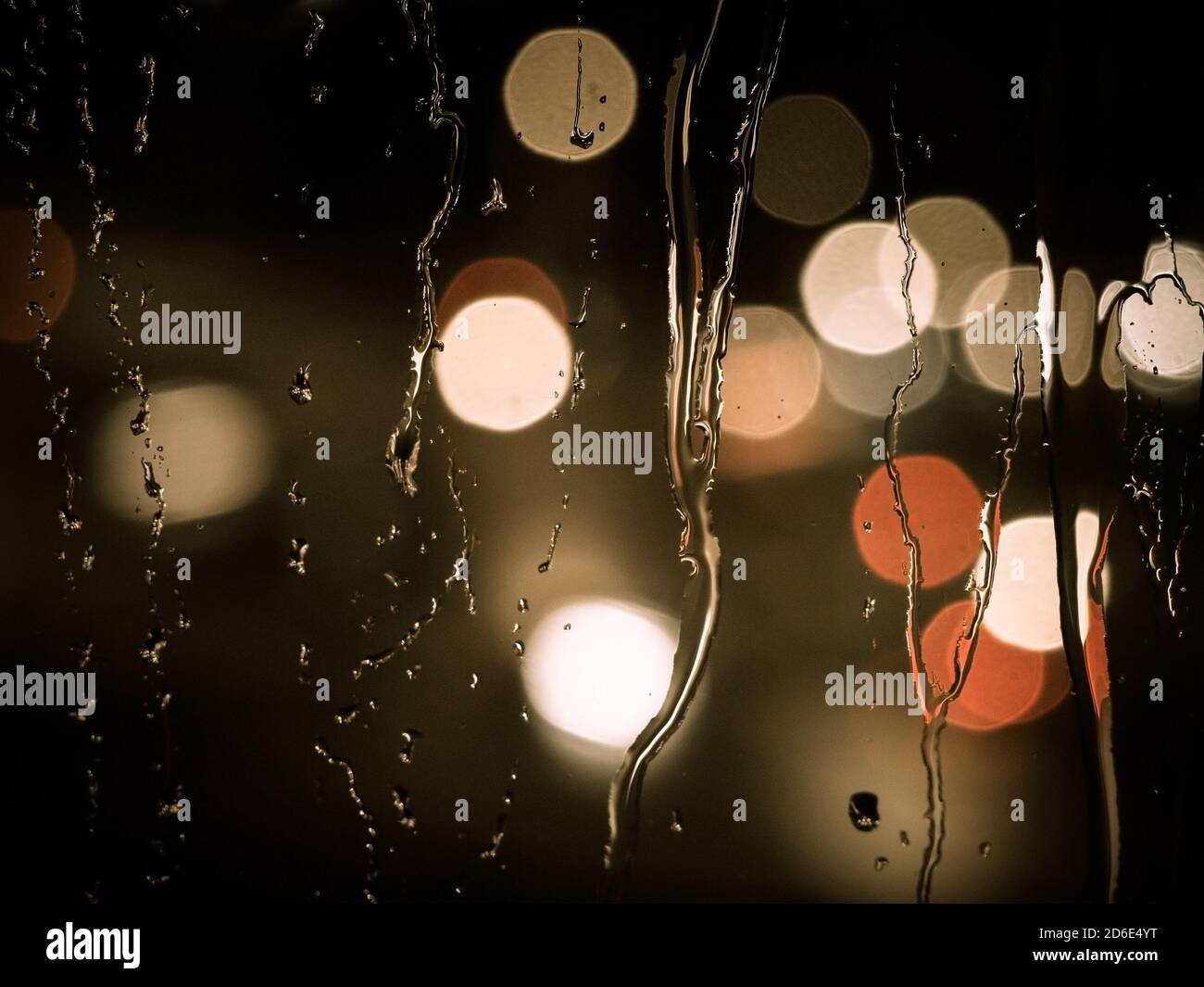 Raindrops and water trickling down a window pane with defocused street ...