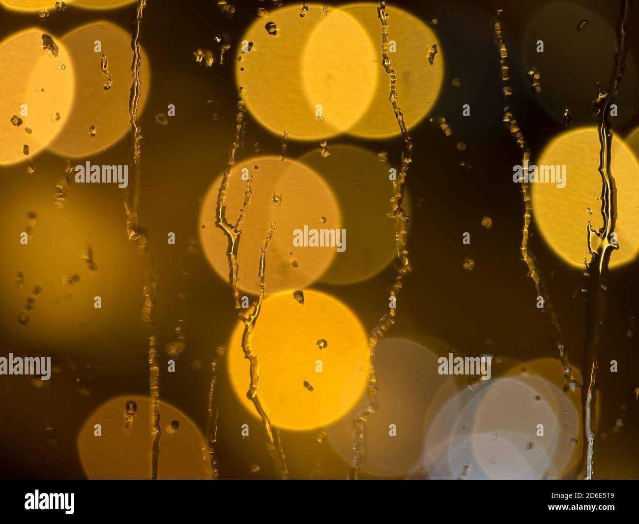 Raindrops and water trickling down a window pane with defocused street ...