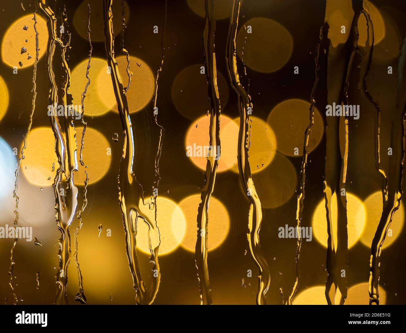 Raindrops and water trickling down a window pane with defocused street ...