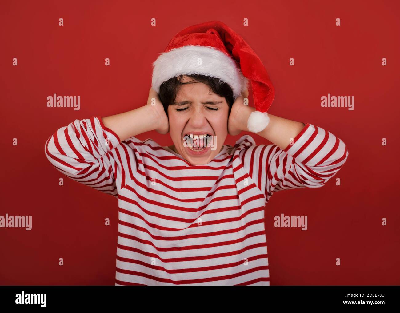 angry kid wearing Santa Claus hat with his hands on his head over red ...