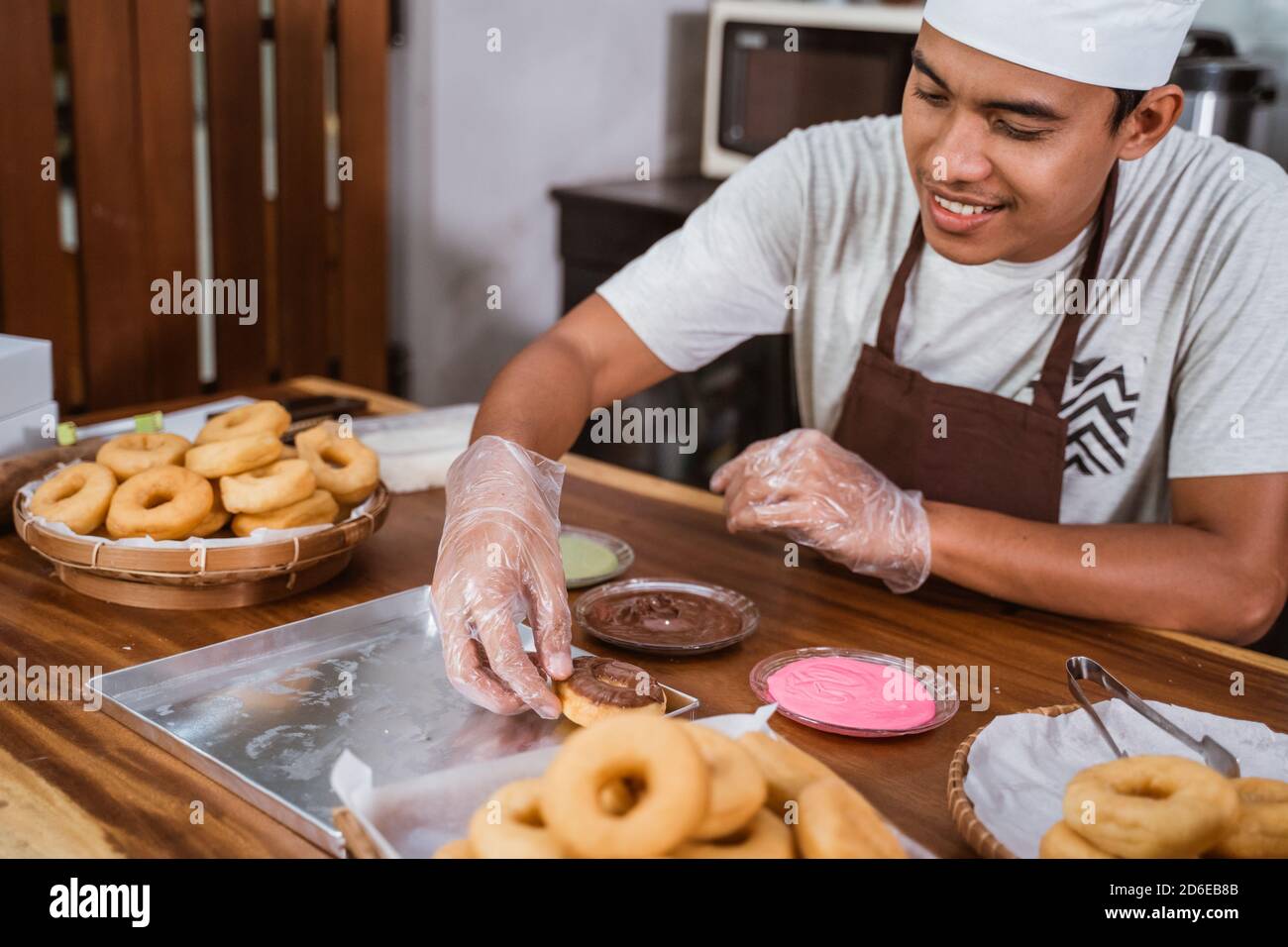 The male chef gives chocolate to decorate donuts in the kitchen, making ...