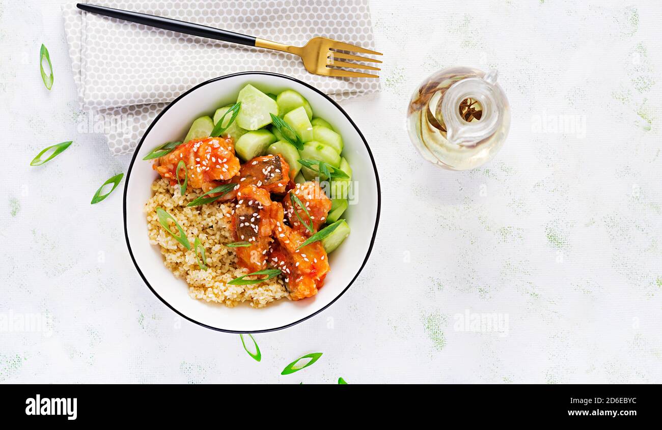 Fish fillet cooked in tomato sauce with bulgur and cucumber on a plate ...