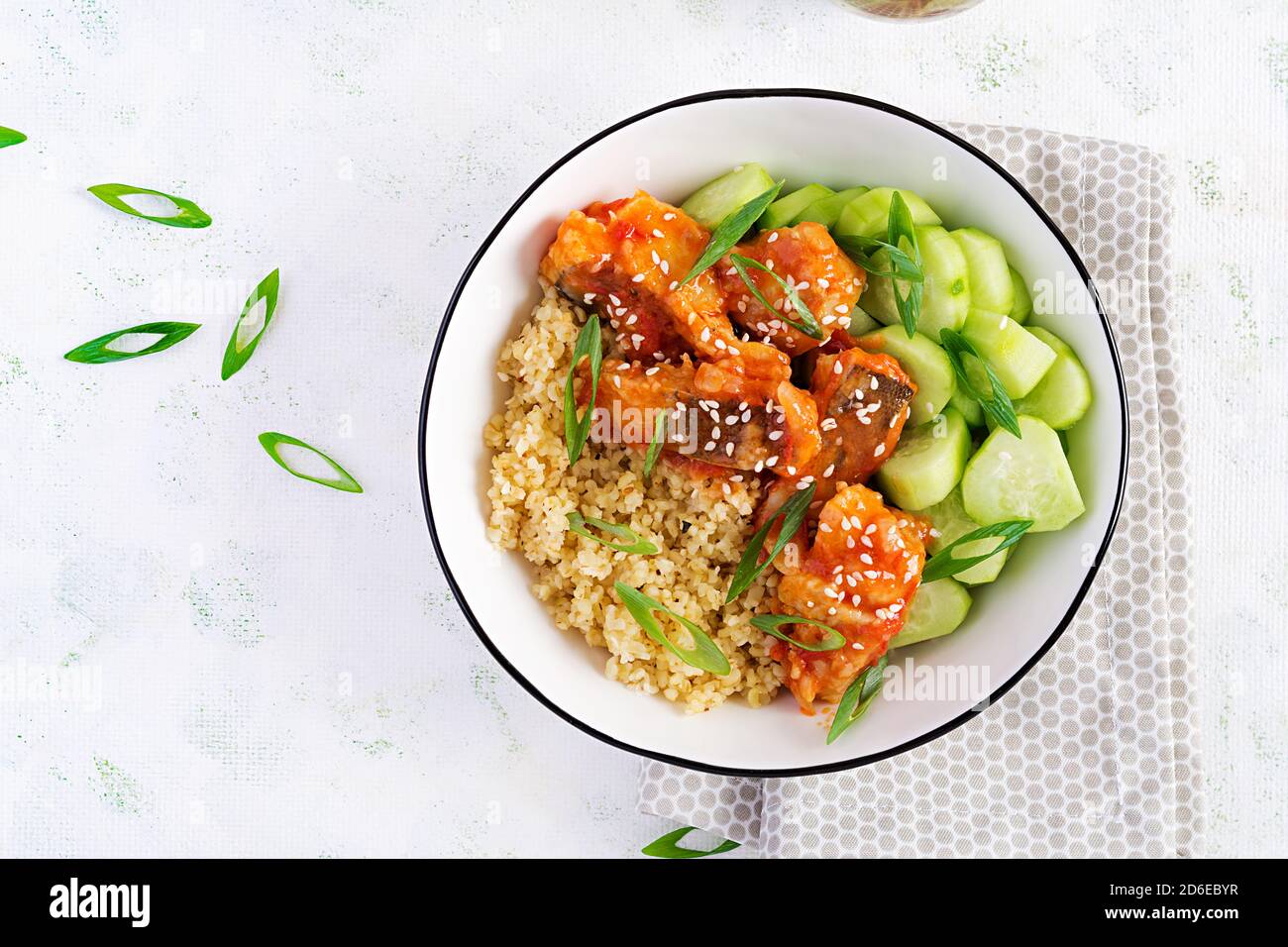 Fish fillet cooked in tomato sauce with bulgur and cucumber on a plate ...