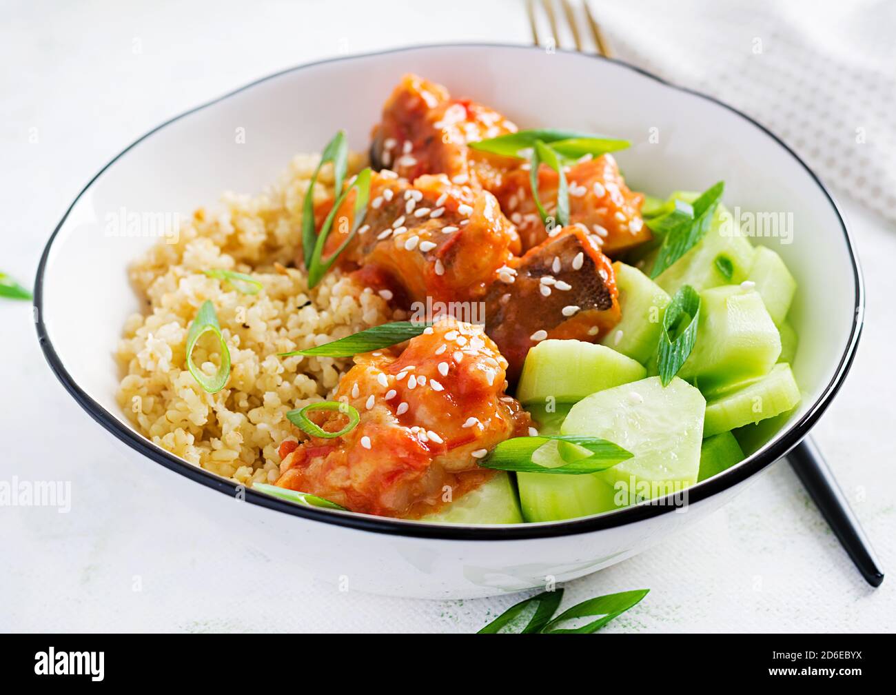 Fish fillet cooked in tomato sauce with bulgur and cucumber on a plate ...