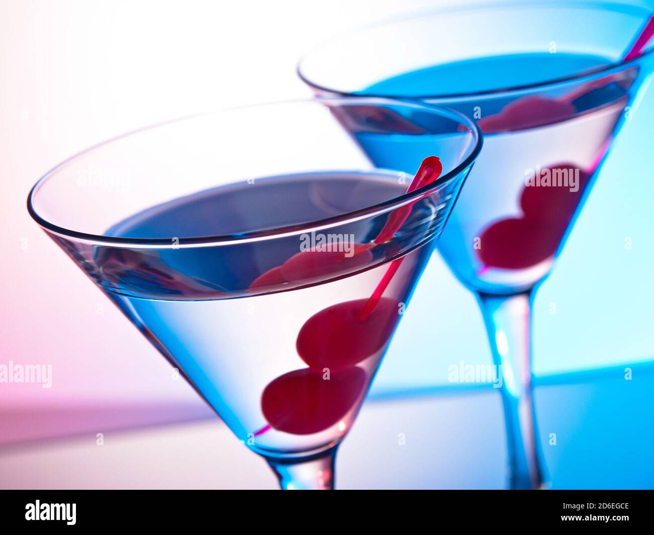 Two glasses of martini with red cherries on a mixed color background ...
