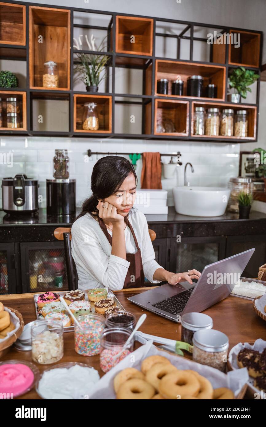 female chef unhappy wearing an apron when using a laptop while sitting ...