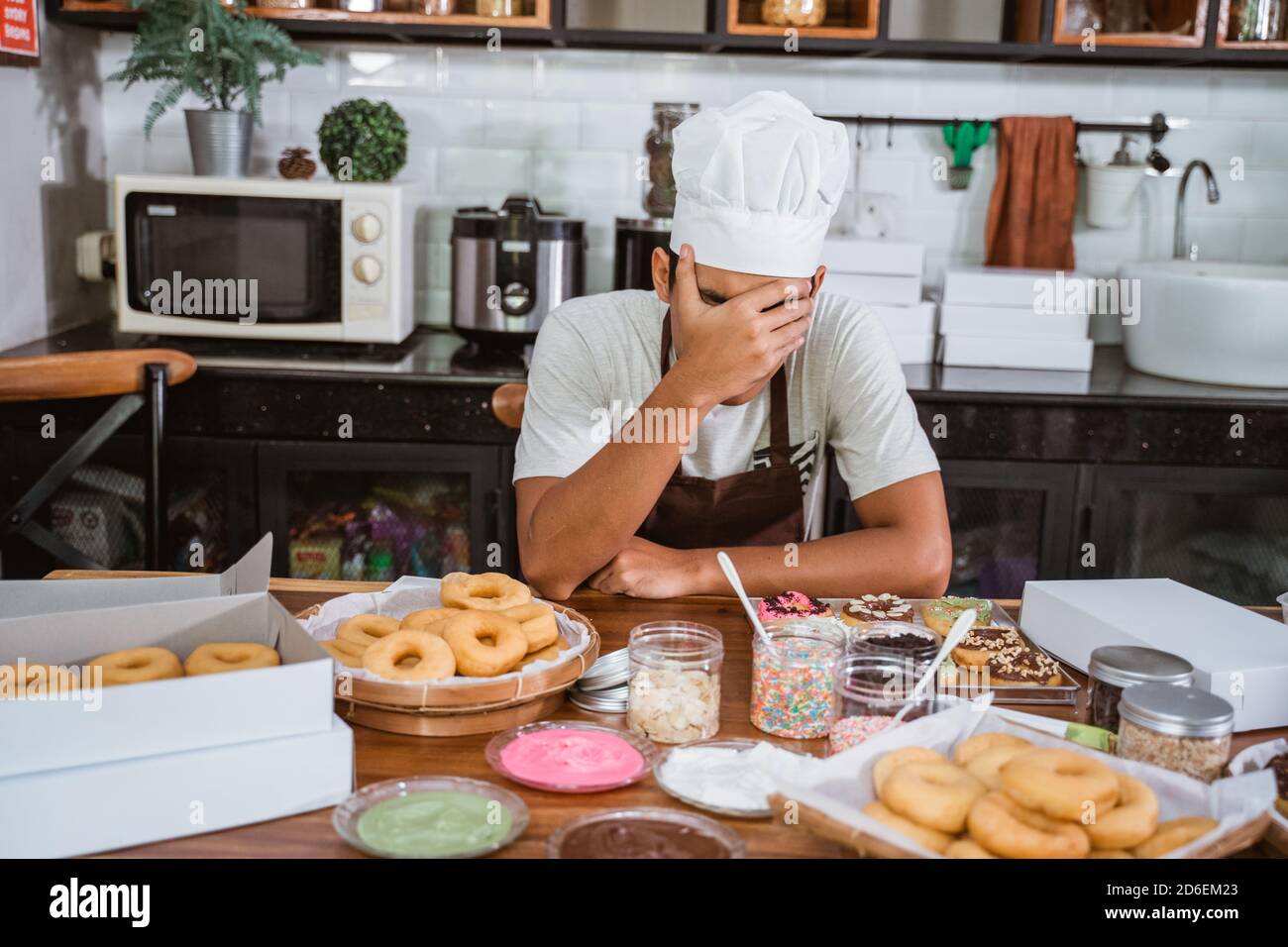 man chef looking unhappy wearing an apron hold a head when sitting in ...