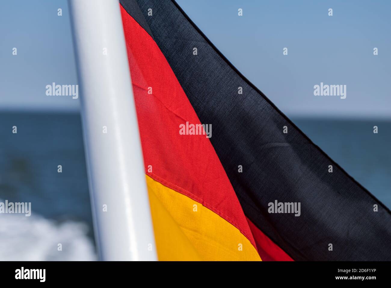 A German flag, waving in the wind, on a ship by the sea. Black, red ...