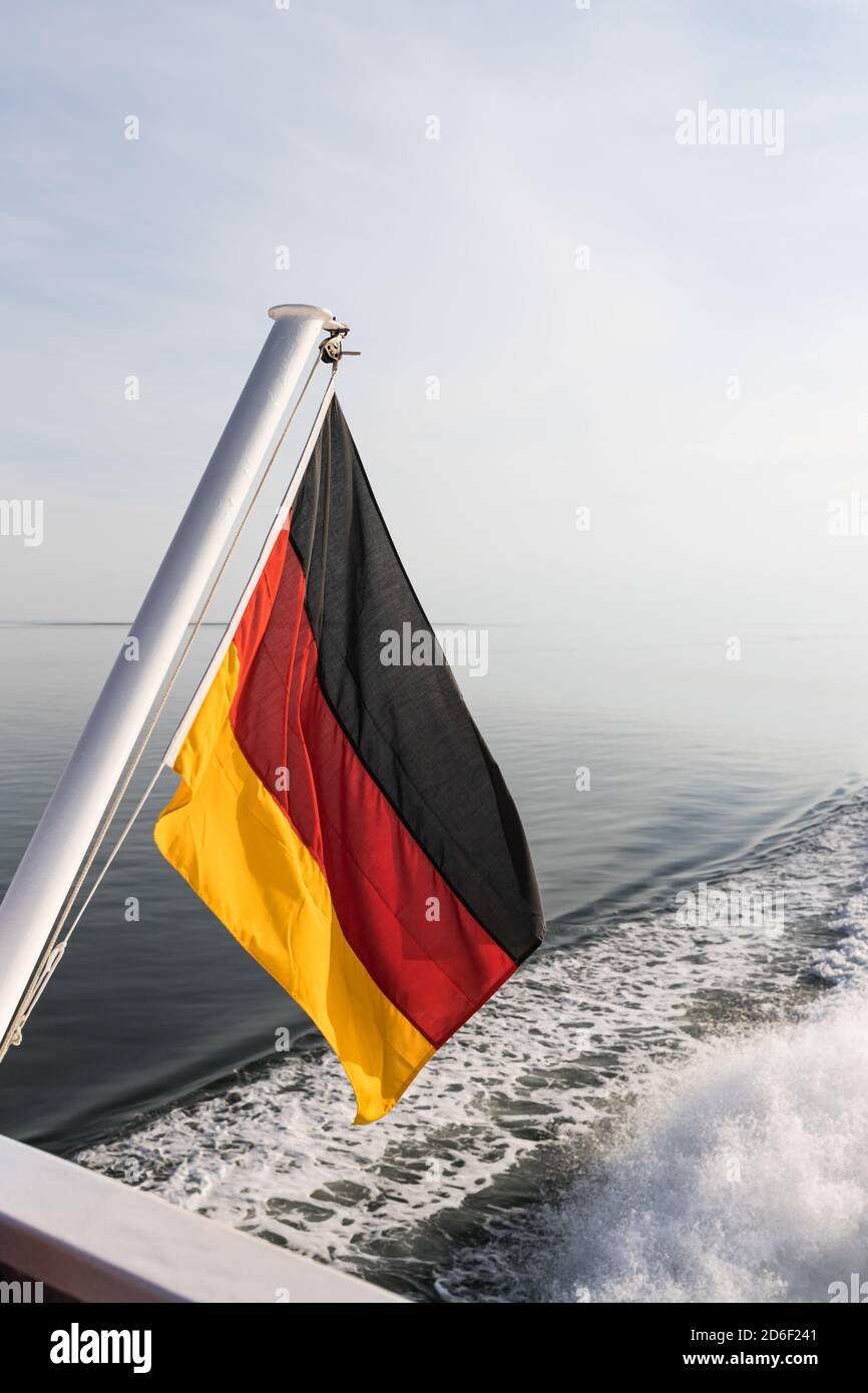 A German flag, waving in the wind, on a ship by the sea. Black, red ...