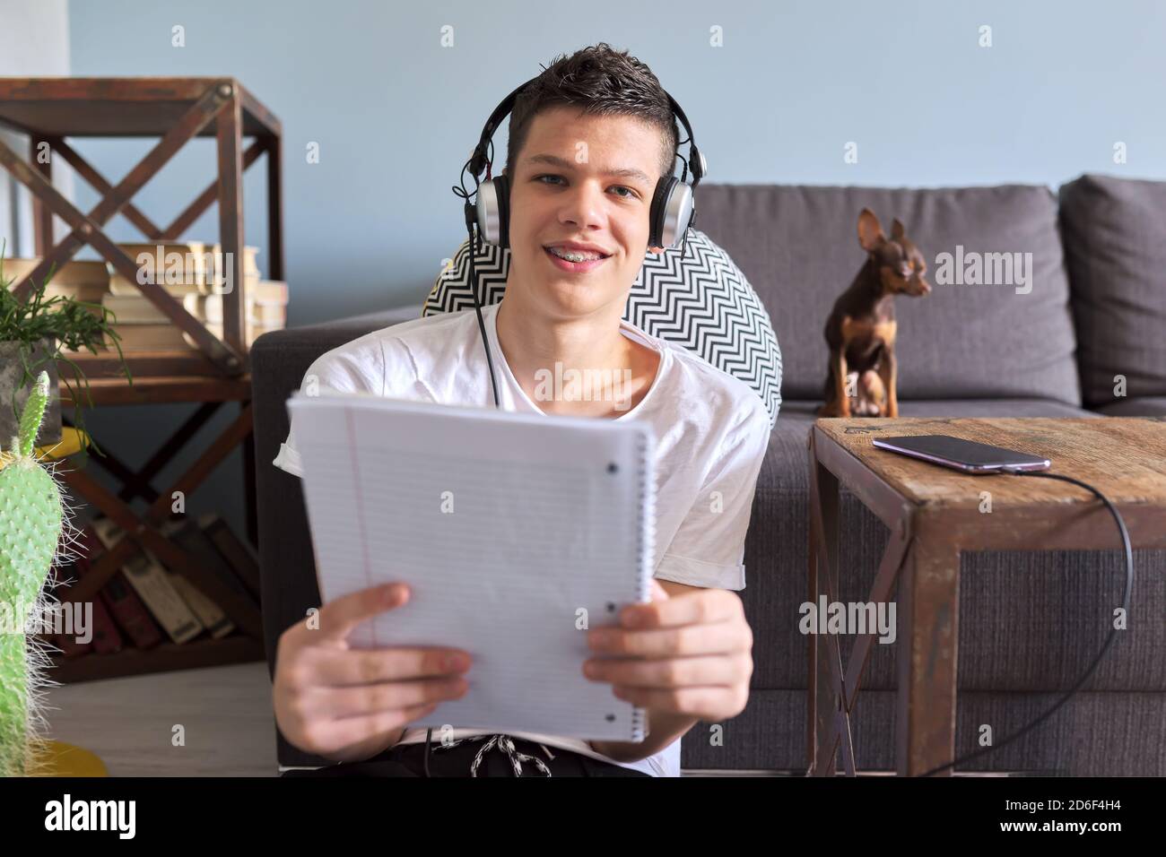 Teenager student in headphones with notebook and smartphone studying ...