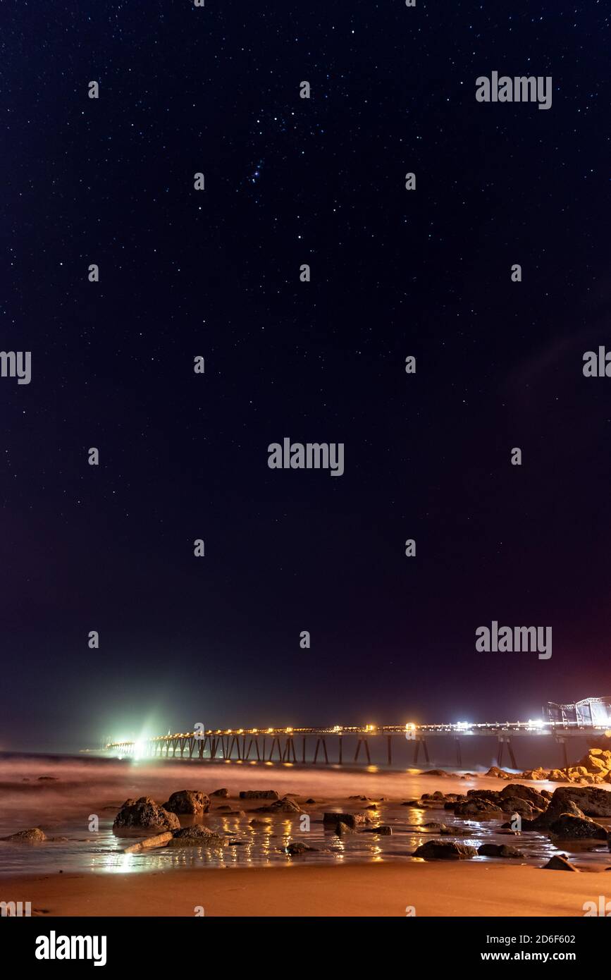 Richfield Pier reflects in the wet rocky sand of Mussel Shoals beach ...