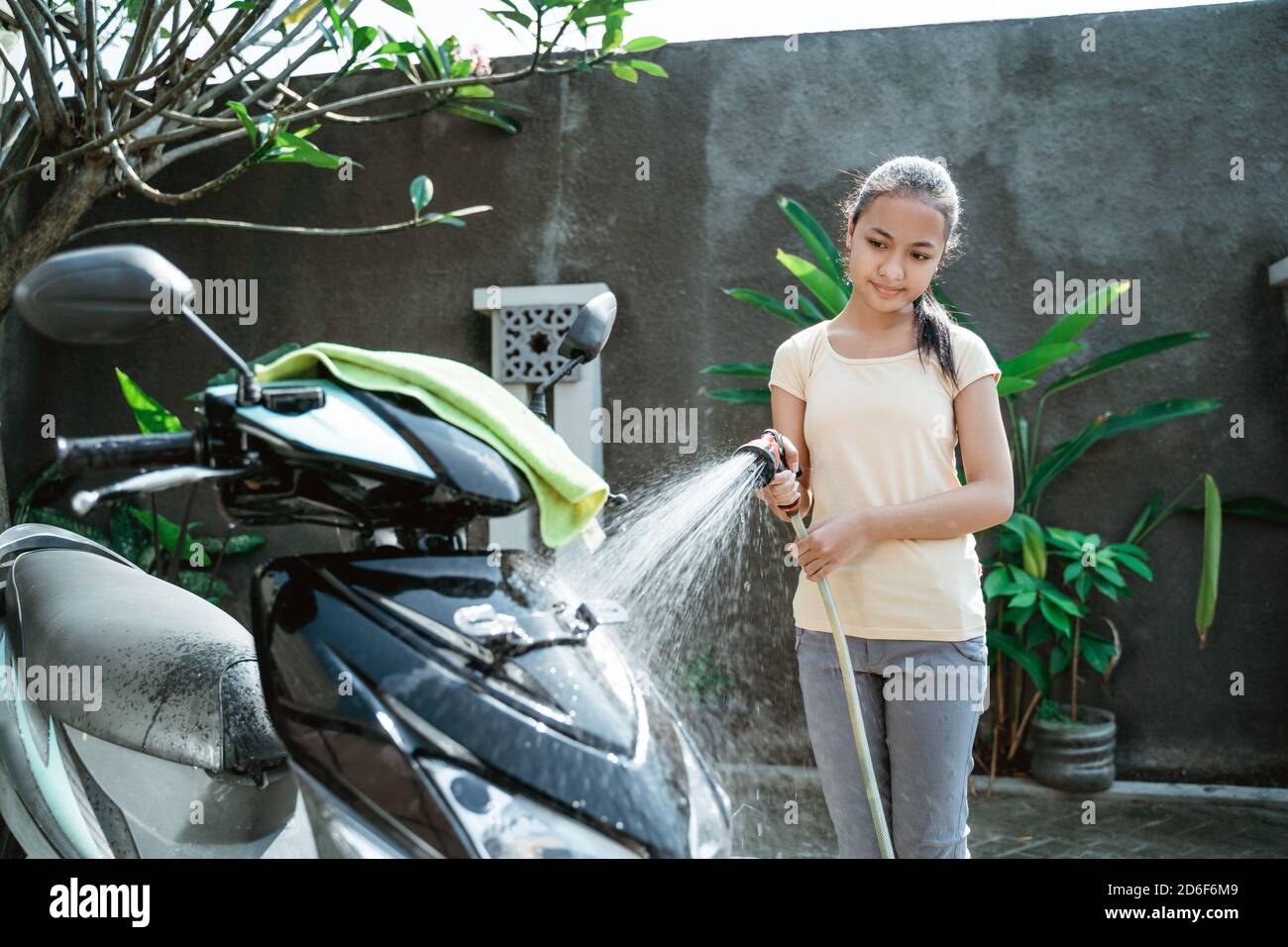 asian young girl washing his motorcycle scooter with water at home ...