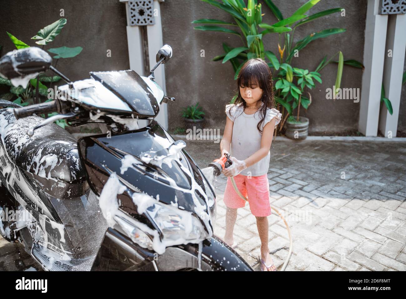 asian young girl washing his motorcycle scooter with water at home ...