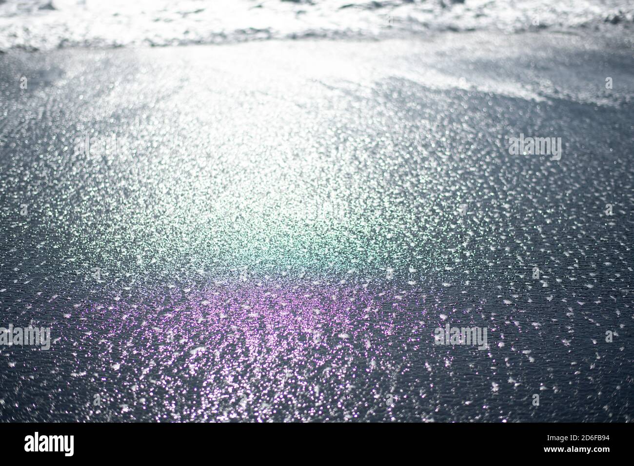 water shimmers on a black sand beach as it recedes back into the ocean ...