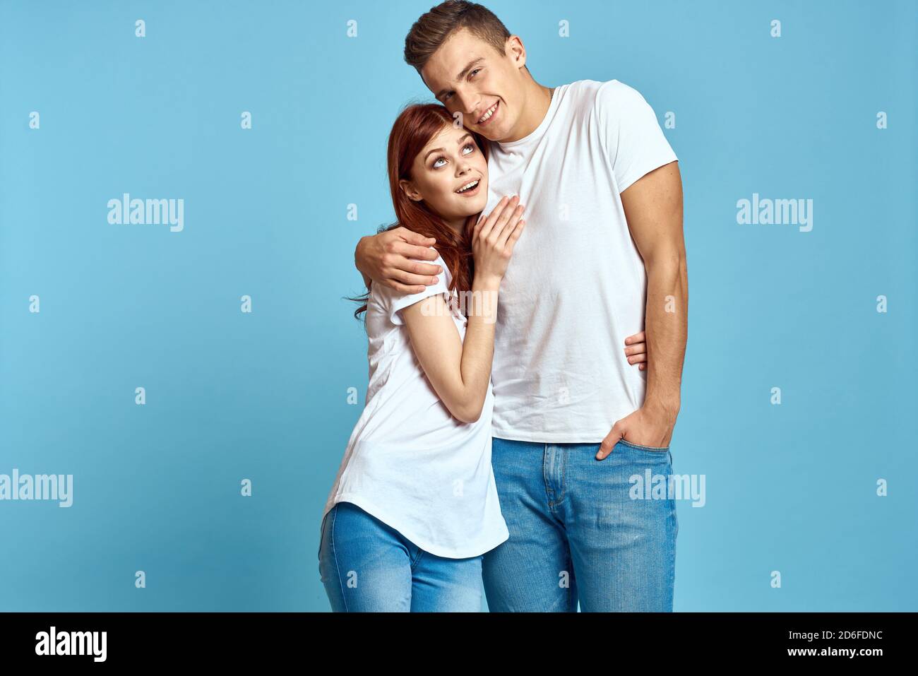enamored man and woman in jeans and a T-shirt on a blue background hug ...