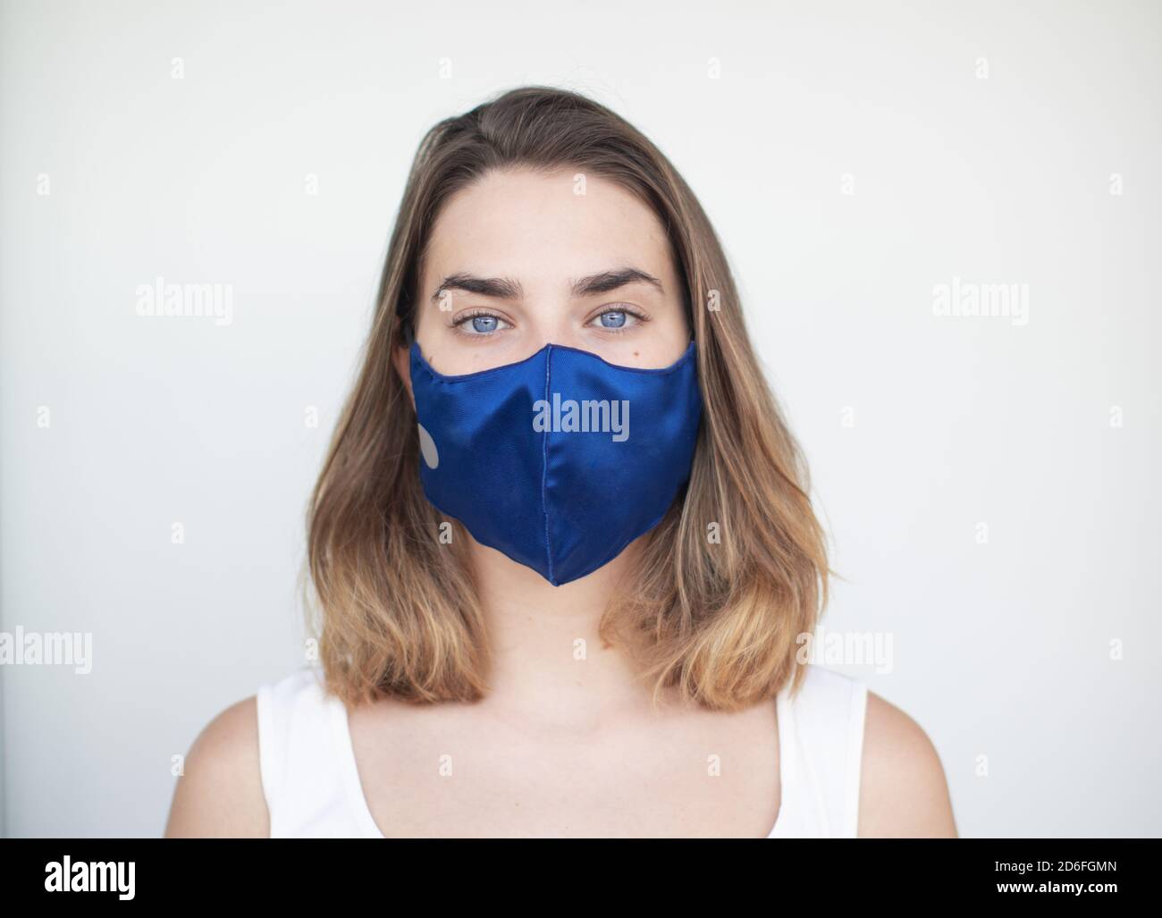 Portrait of a young female with blue eyes wearing a blue facemask ...