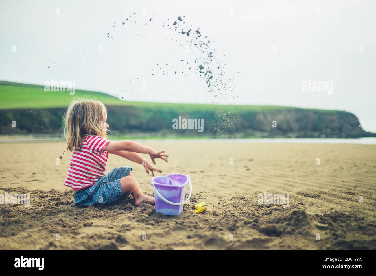 A little preschooler is sitting on the beach and is throwing sand Stock ...