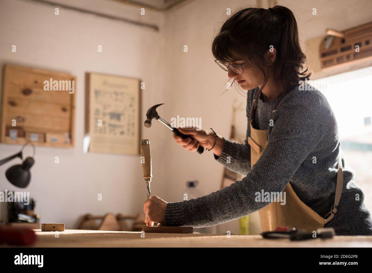 A young female carpenter working as wood designer in a small carpentry ...