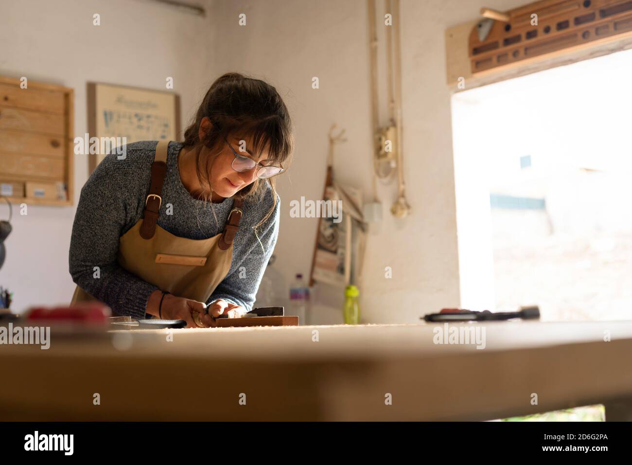 A young female carpenter working as wood designer in a small carpentry ...