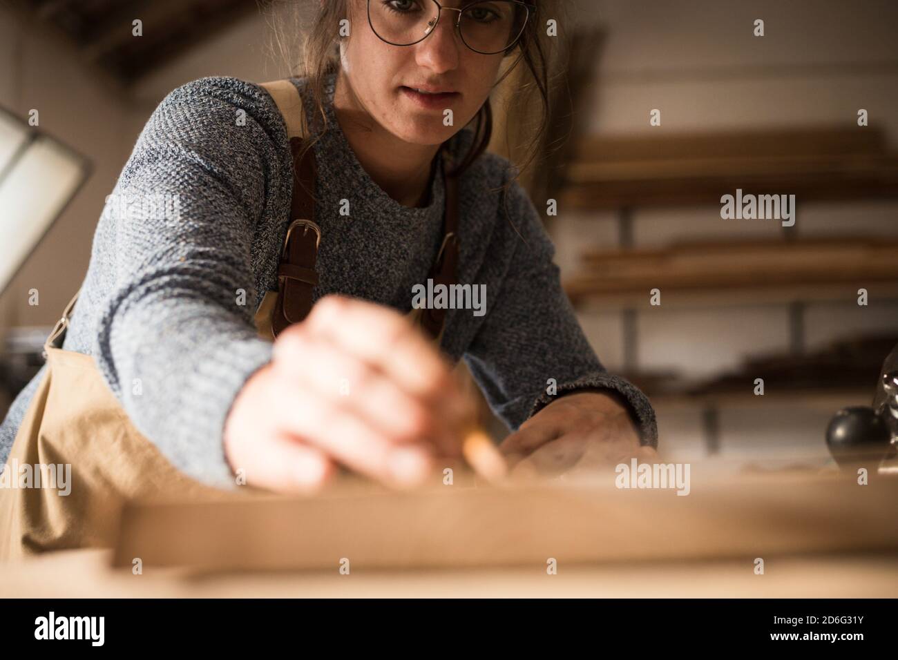 A young female carpenter working as wood designer in a small carpentry ...
