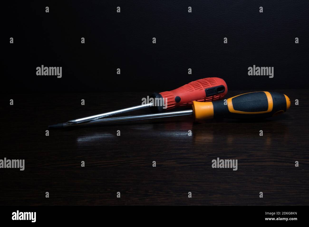 Two screwdrivers of different colors with reflection lying on a dark ...