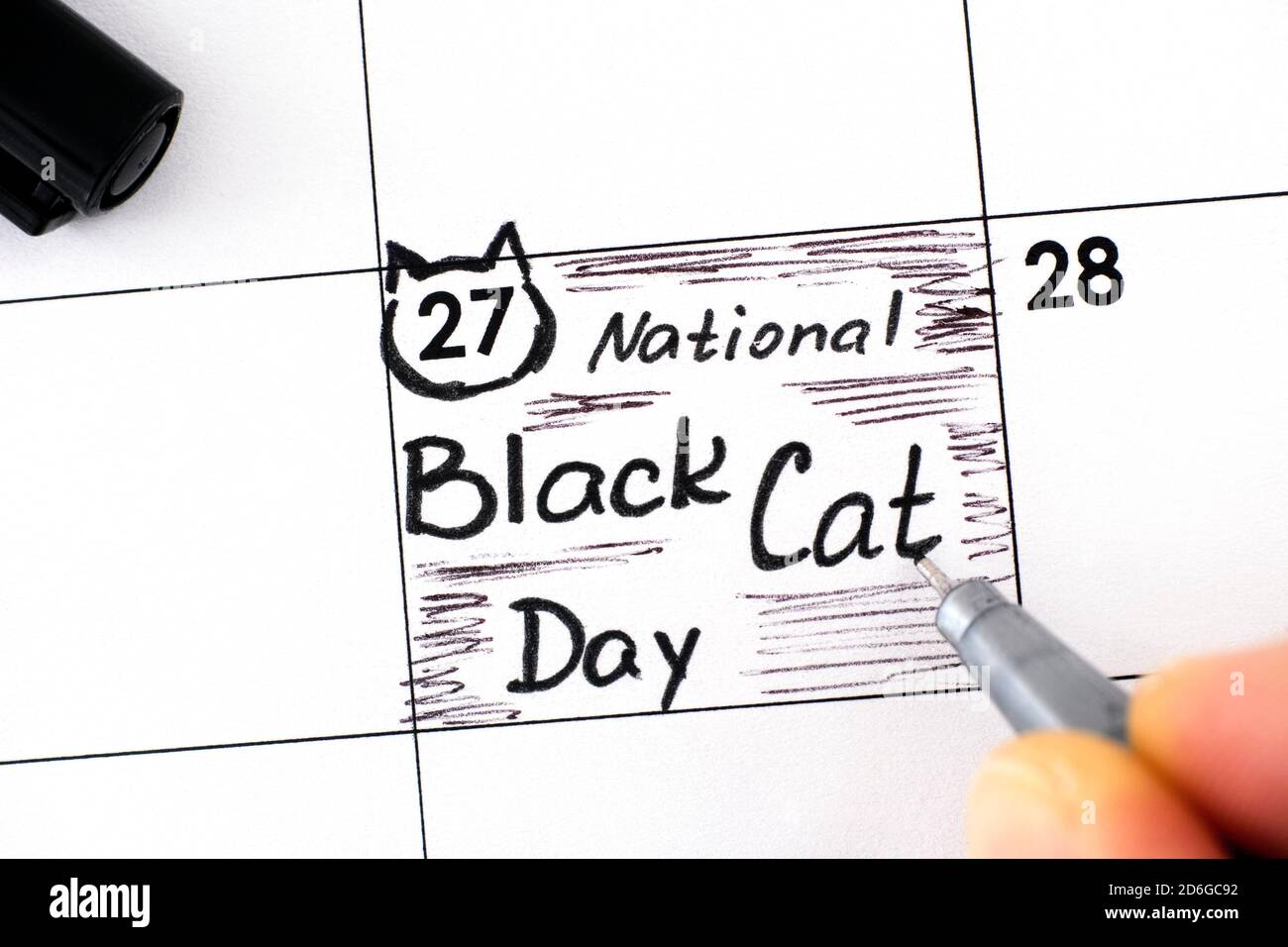 Woman fingers with pen writing reminder National Black Cat Day in ...