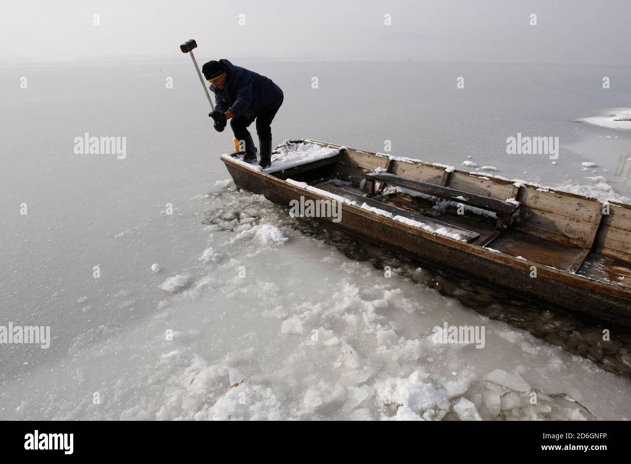 Fisherman breaking ice on surface of the frozen lake Stock Photo - Alamy