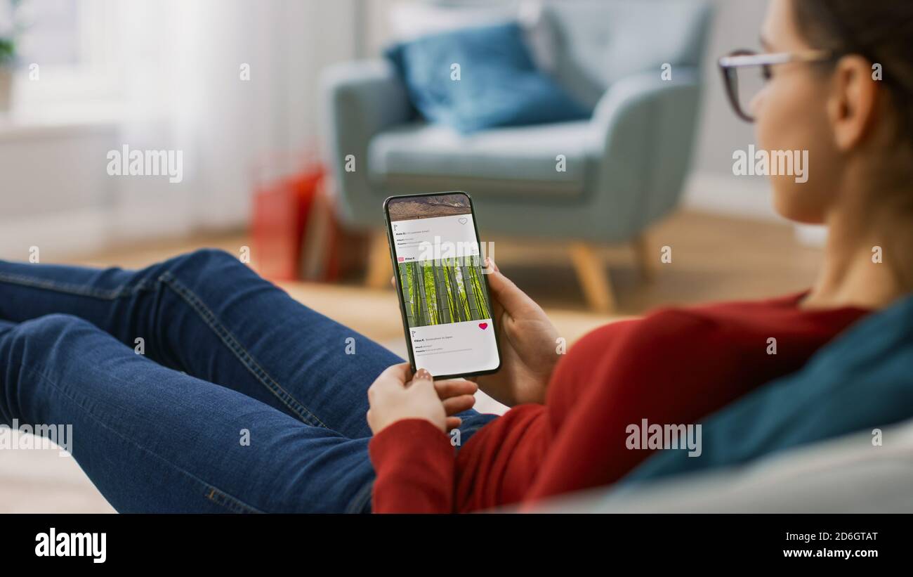 Young Woman at Home Lying on a Couch using Smartphone Scrolling Through Sotcial Media Feed ...