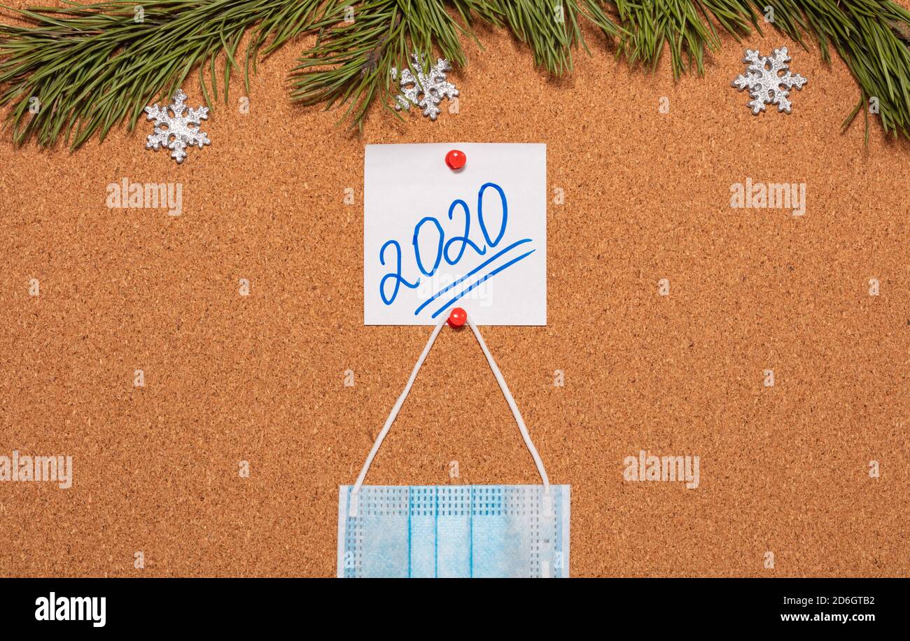 Medical mask and white sticky note with 2020 pinned on notice board ...