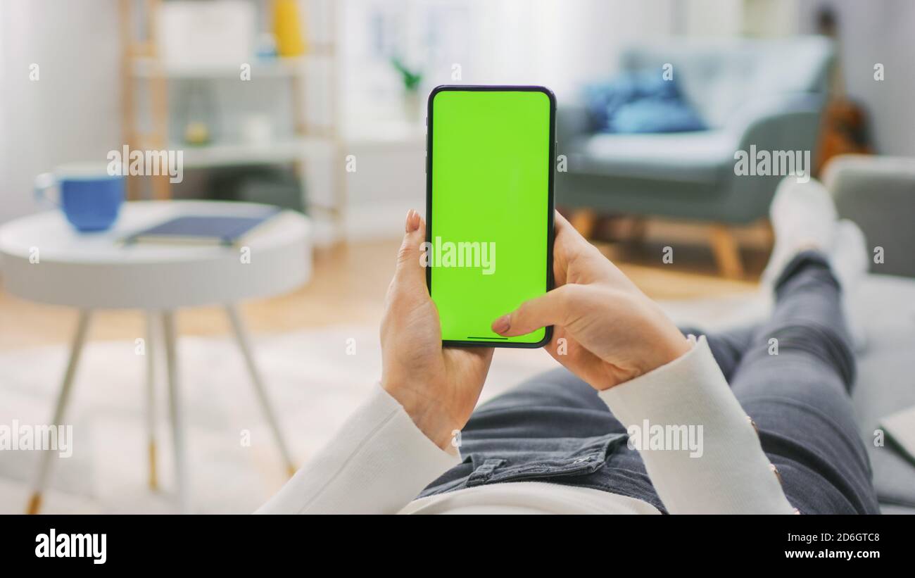 Woman at Home Lying on a Couch using Smartphone with Green Mock-up Screen, Doing Swiping ...