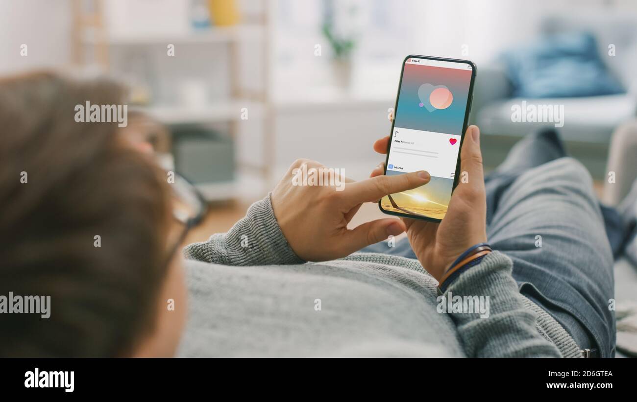 Man at Home Lying on a Couch using Smartphone, Scrolling Social Media Feed, Checking News ...