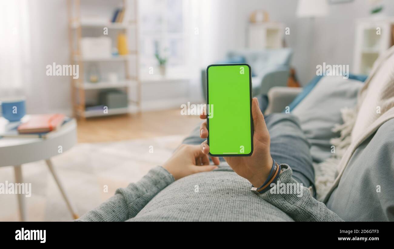 Man at Home Lying on a Couch using Smartphone with Green Mock-up Screen, Doing Swiping ...