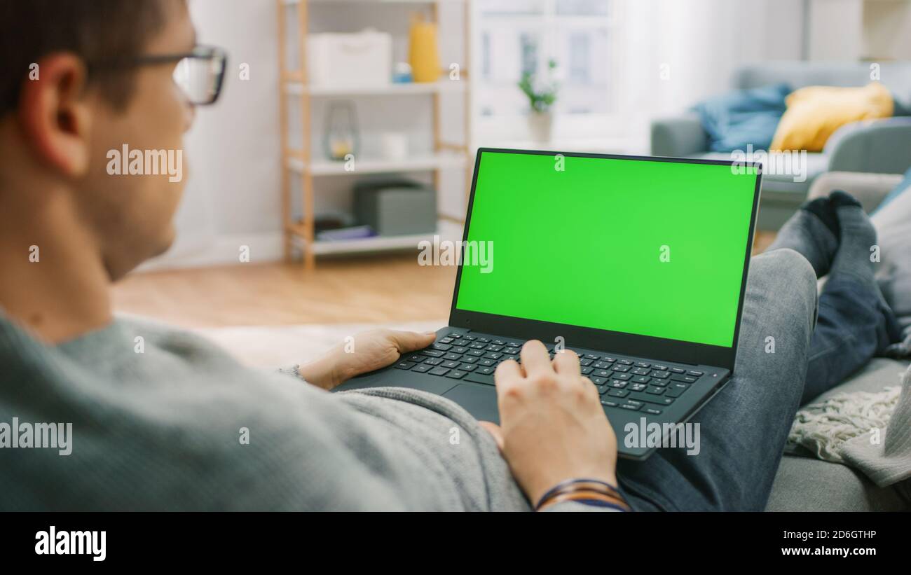 Man at Home Sitting on a Couch Working on Green Mock-up Screen Laptop Computer. Guy Using Laptop ...