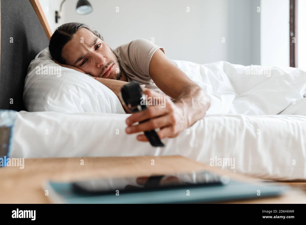 Exhausted tired man being awakened by an alarm clock in his bedroom ...