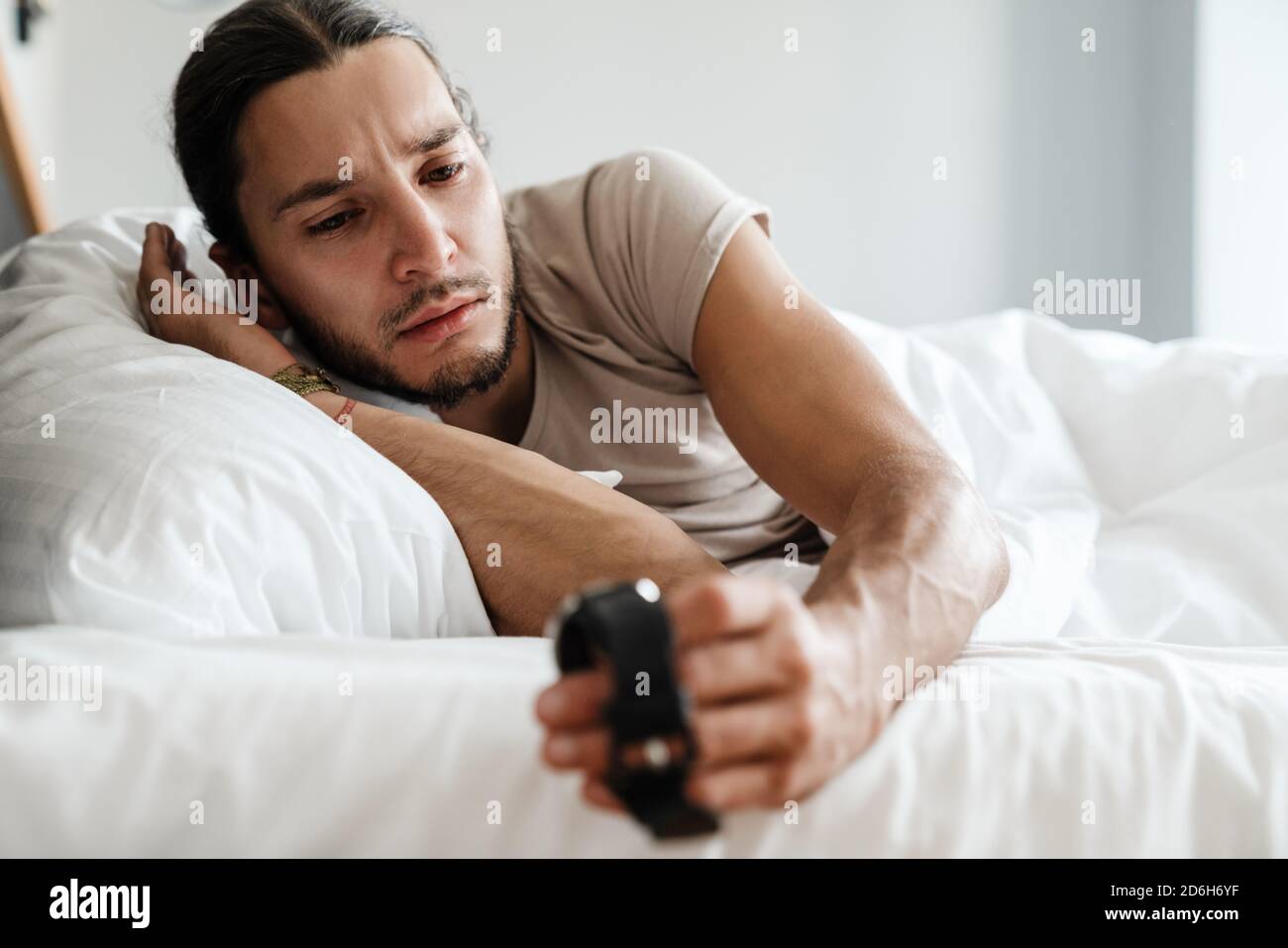 Exhausted tired man being awakened by an alarm clock in his bedroom ...