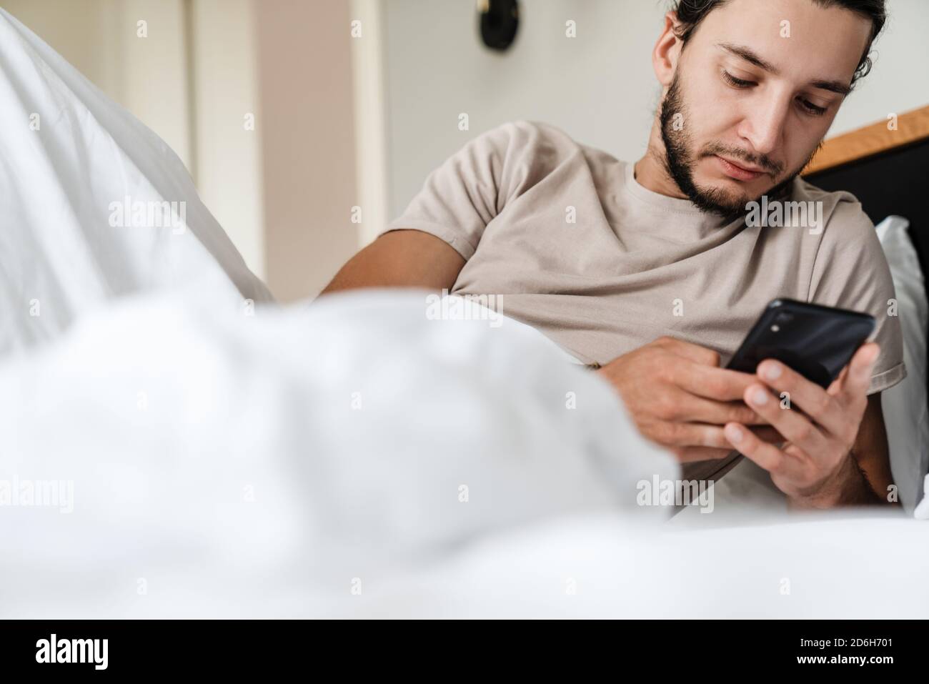 Tired sleepy young man using mobile phone while laying in bed in the ...