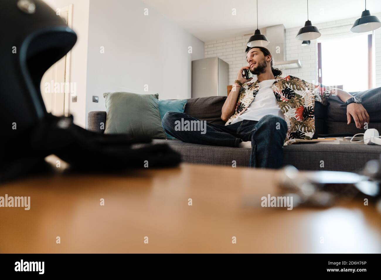 Smiling young man making a phone call while sitting on a couch in his ...