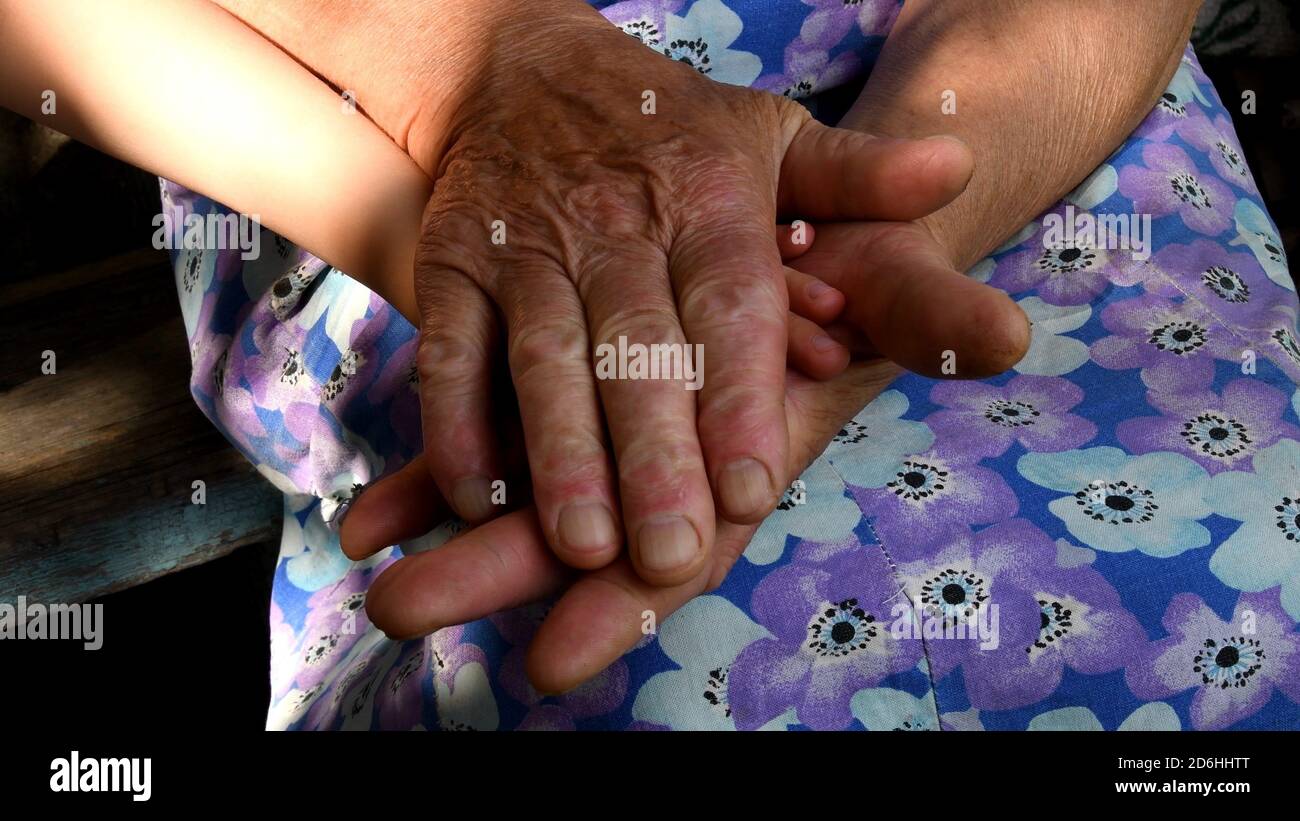Elder woman hold child hand by her wrinkled aged hands. Diverse hands ...