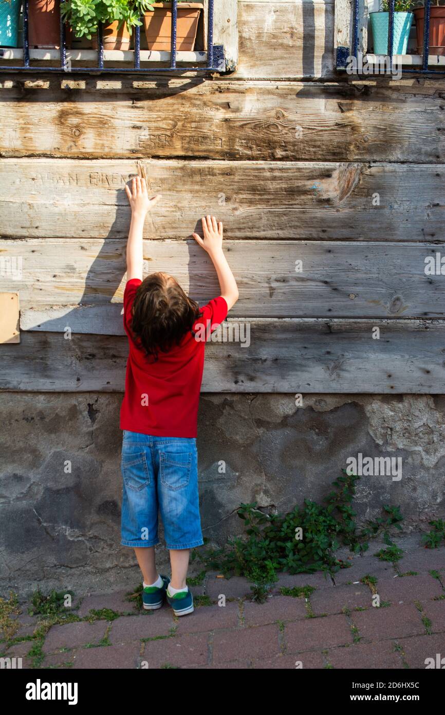 Vertical back view of a male child reaching for a window on a wooden ...
