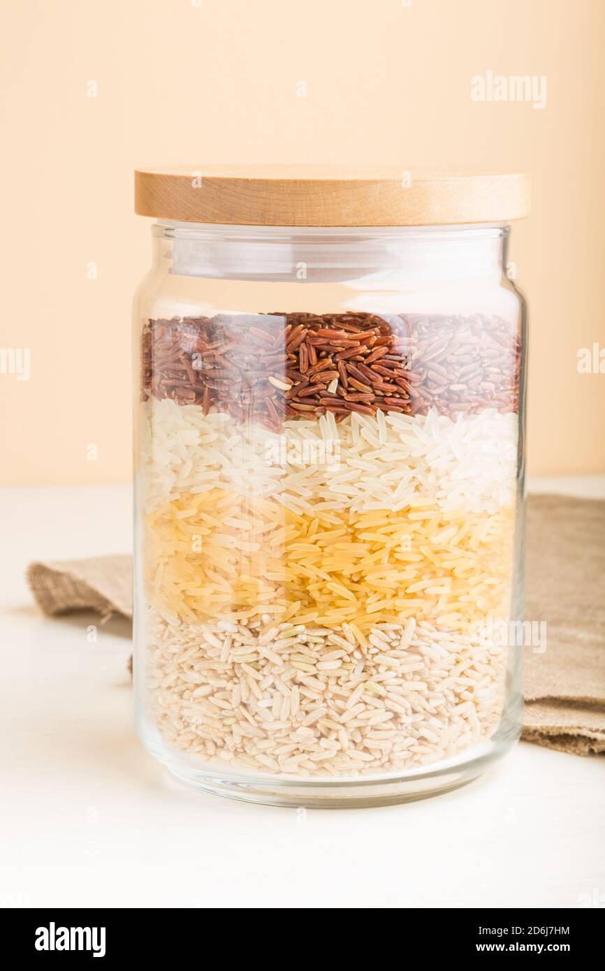 glass jar with different kinds of rice poured in layers on white and ...