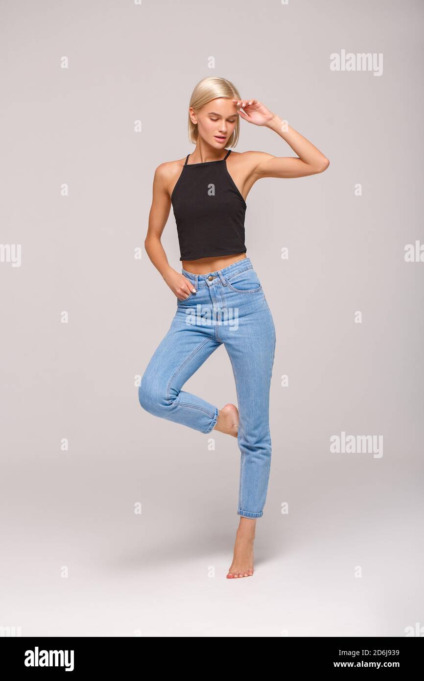 Freestyle. Young blonde woman in jeans and top standing on one leg ...